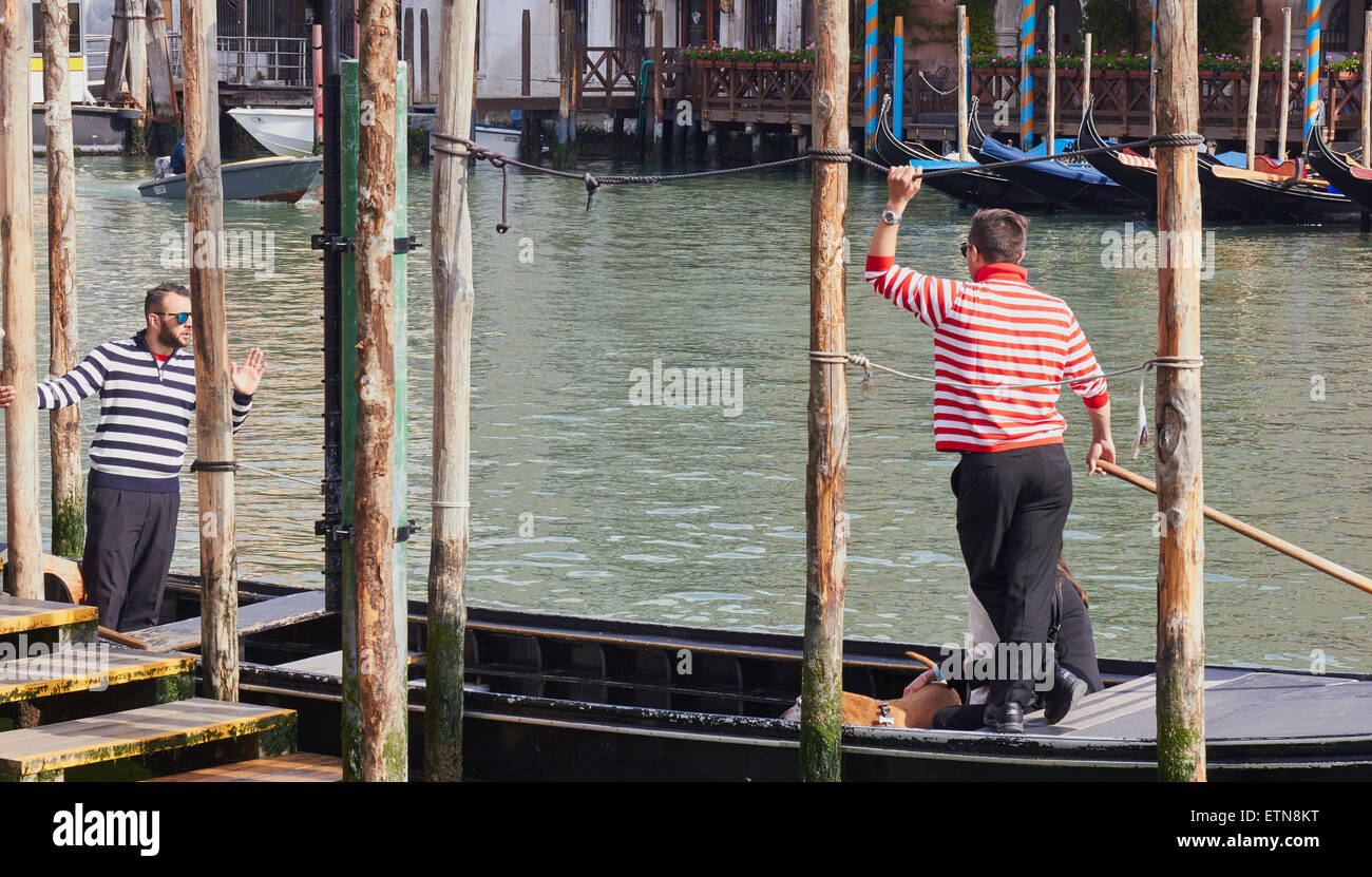Two gondoliers in striped tops preparing to row a traghetto cross the ...