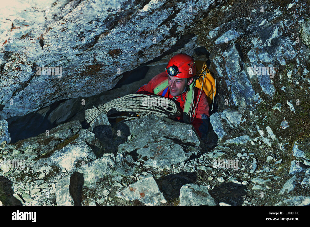 Cave explorer with rope in hand crawls through a constriction in a cave ...