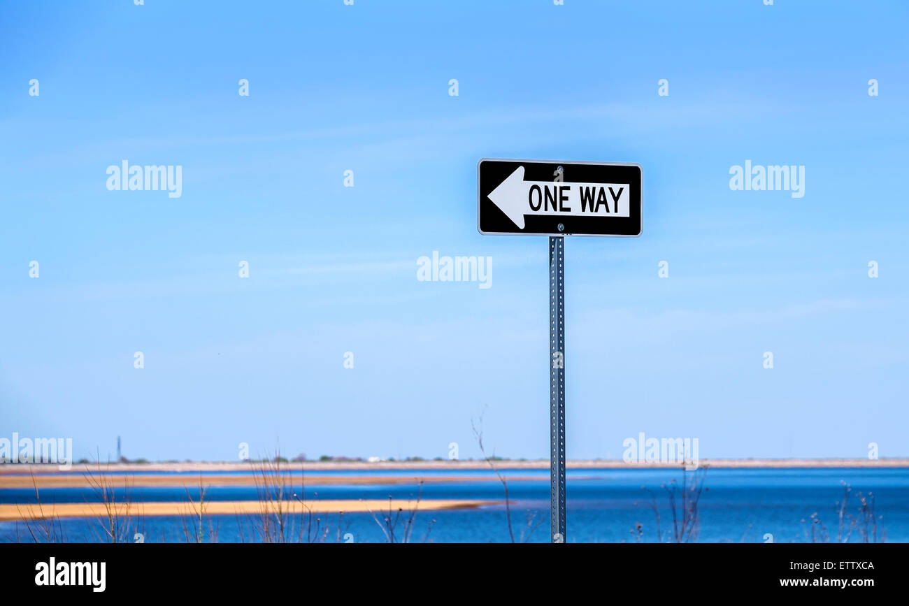 A one way sign on a pole next to a lake, blue sky. USA. Conceptual ...