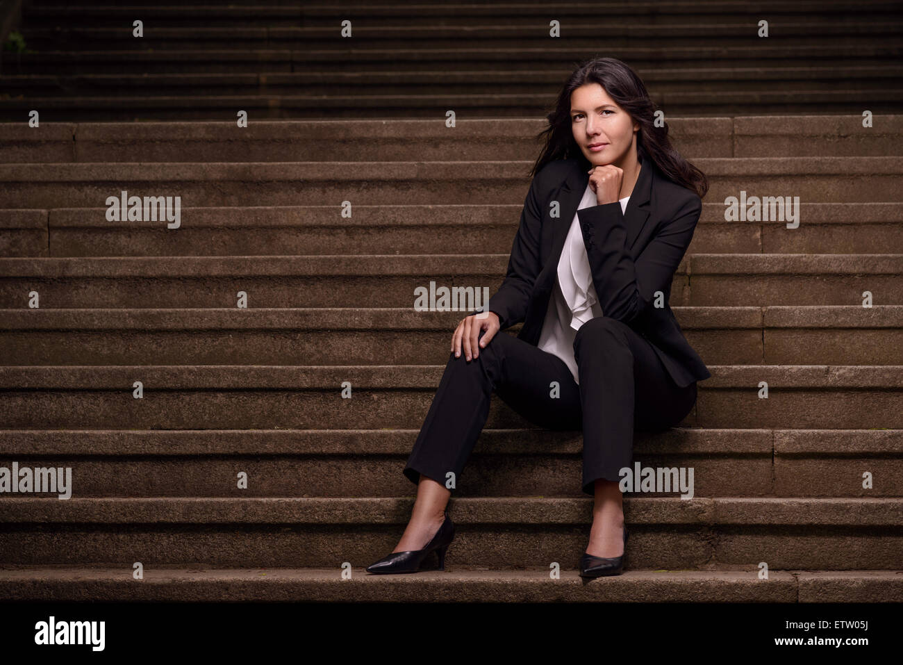Smiling stylish woman in a dark slack suit sitting on a flight of ...