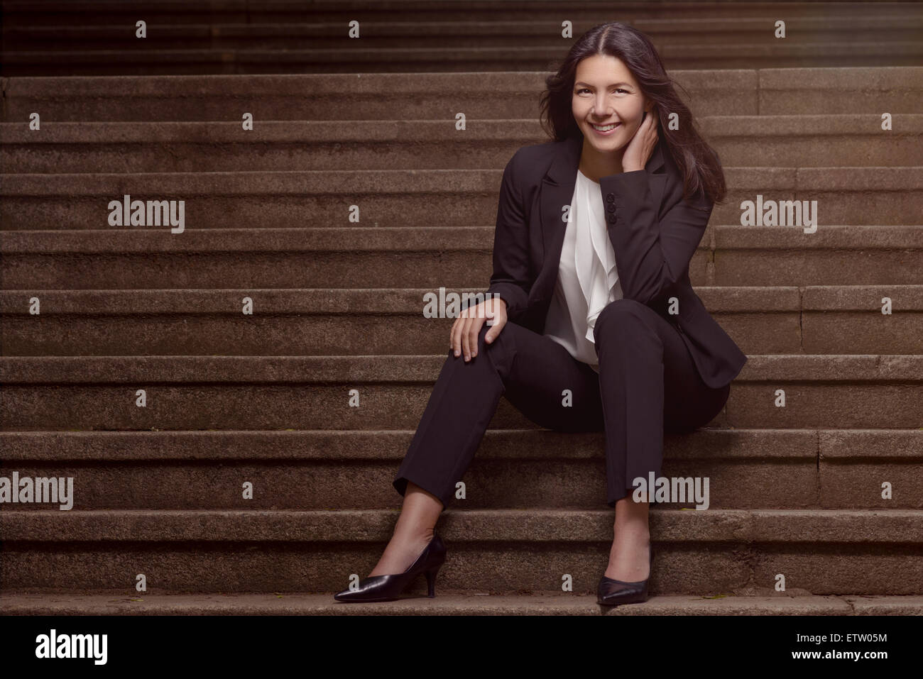 Smiling stylish woman in a dark slack suit sitting on a flight of ...