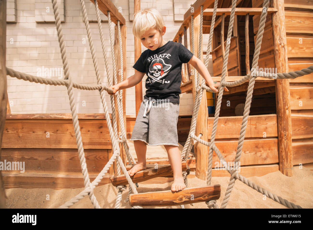 Little boy walking along hanging bridge of wooden ship on playground ...