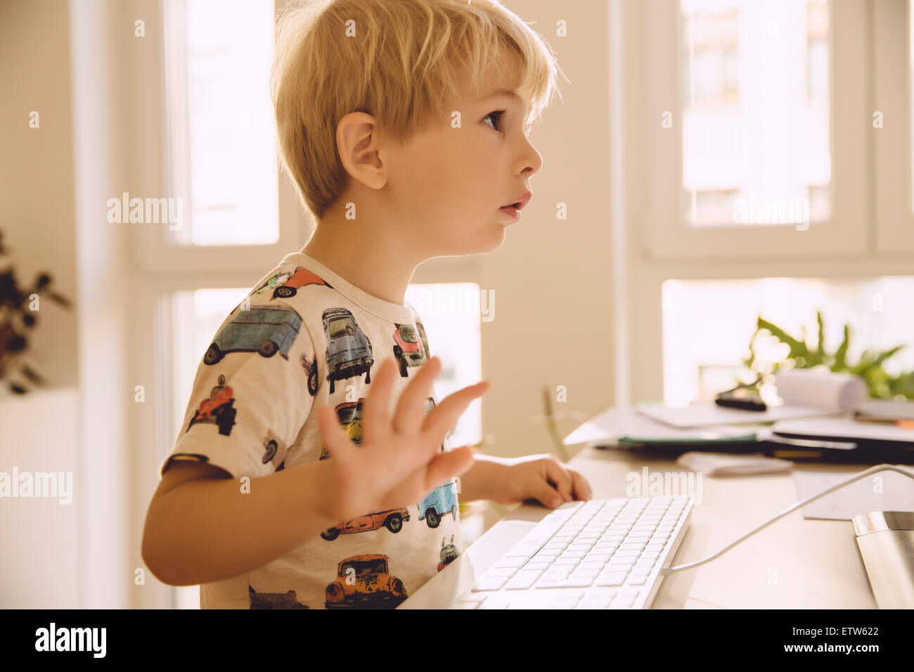 Blond little boy typing on the keyboard of a computer looking at the ...