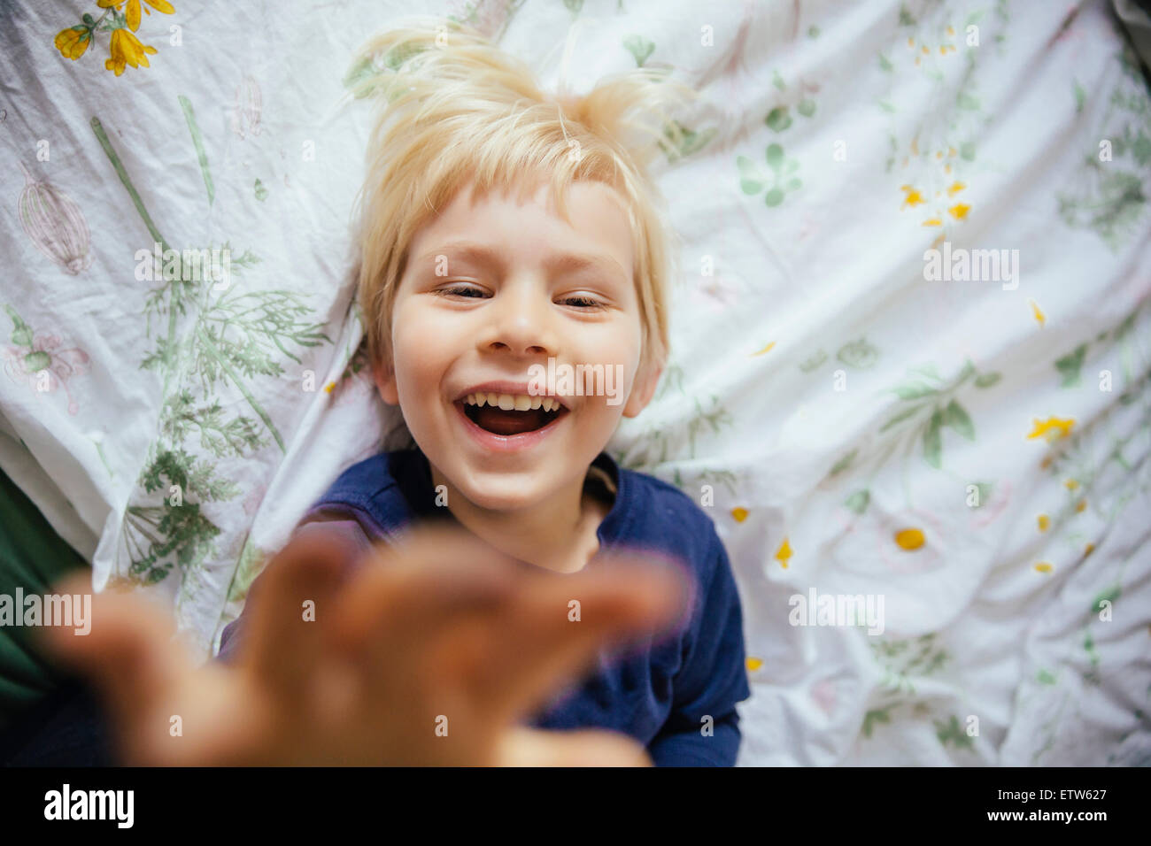Smiling little boy lying on bed reaching out to camera Stock Photo - Alamy