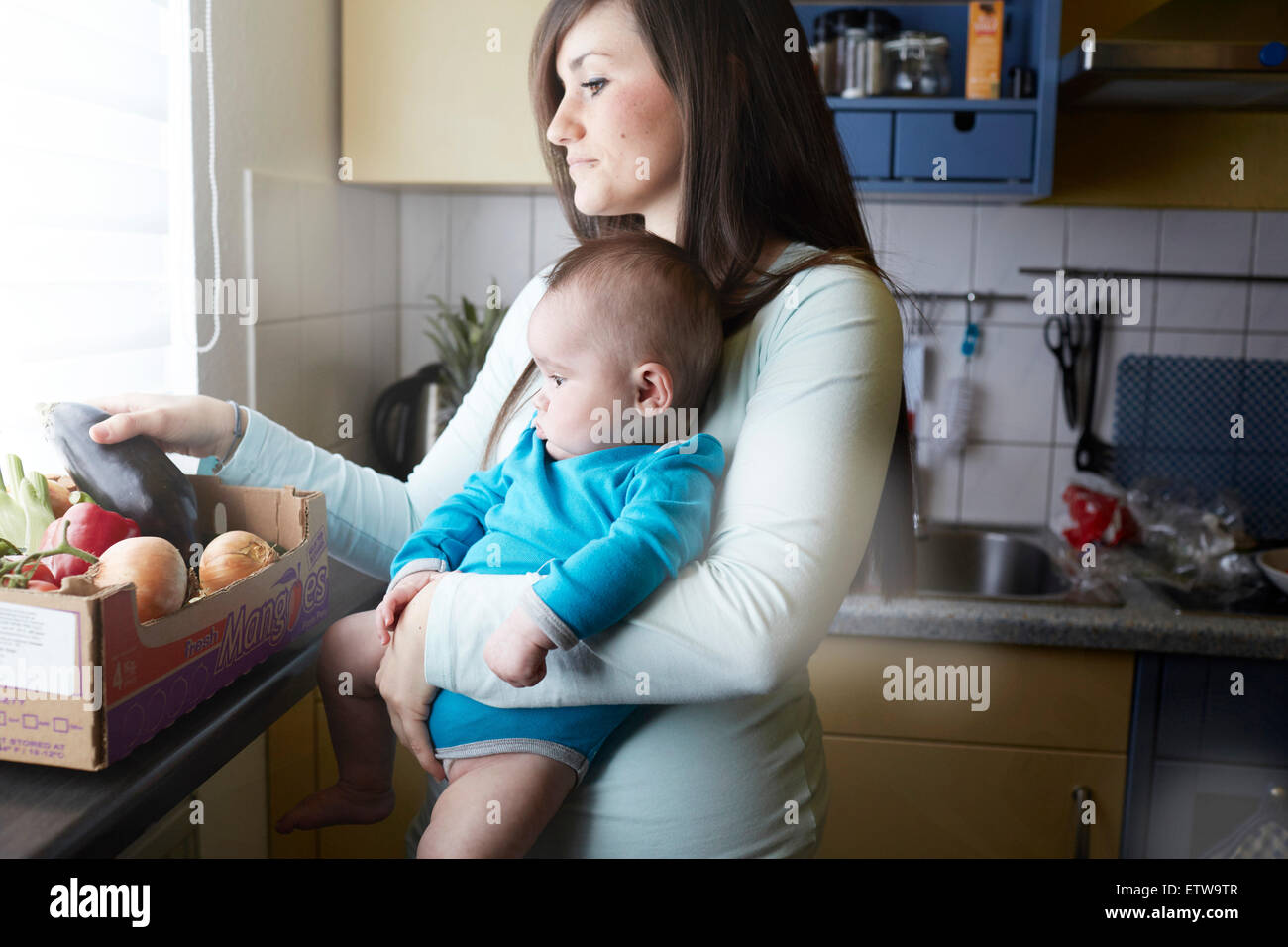 Young mother holding baby in kitchen Stock Photo - Alamy