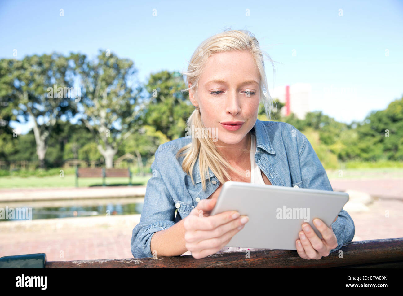 Young woman using digital tablet on park bench Stock Photo - Alamy