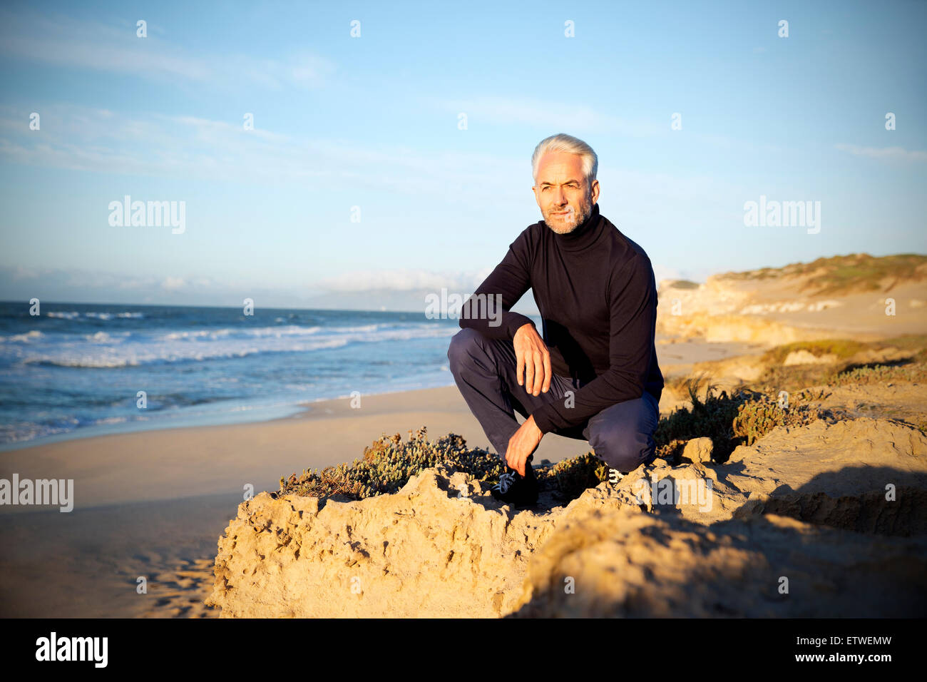 South Africa, man crouching on rocks at the beach before sunrise Stock ...