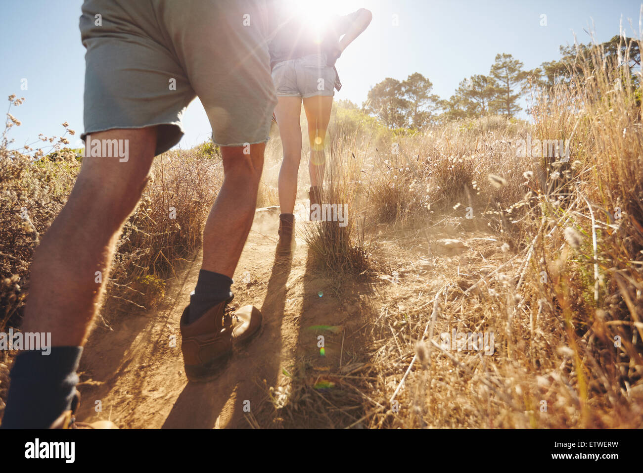 Rear view of two people going uphill on a mountain trail on hot summer ...