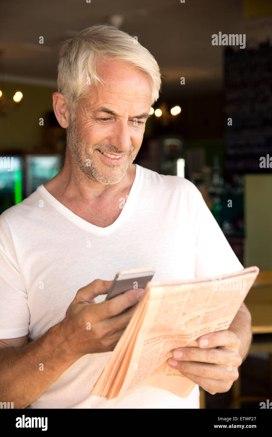 Portrait of smiling man with smartphone reading a newspaper Stock Photo ...