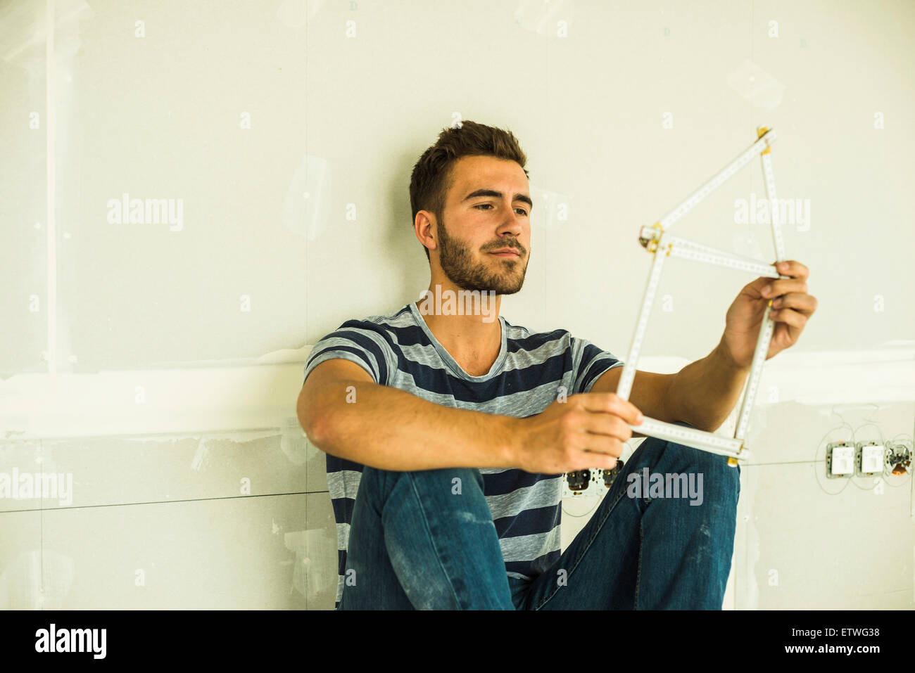 Young man sitting at blank wall holding pocket rule Stock Photo - Alamy Young man sitting at blank wall holding pocket rule Stock Photo - Alamy