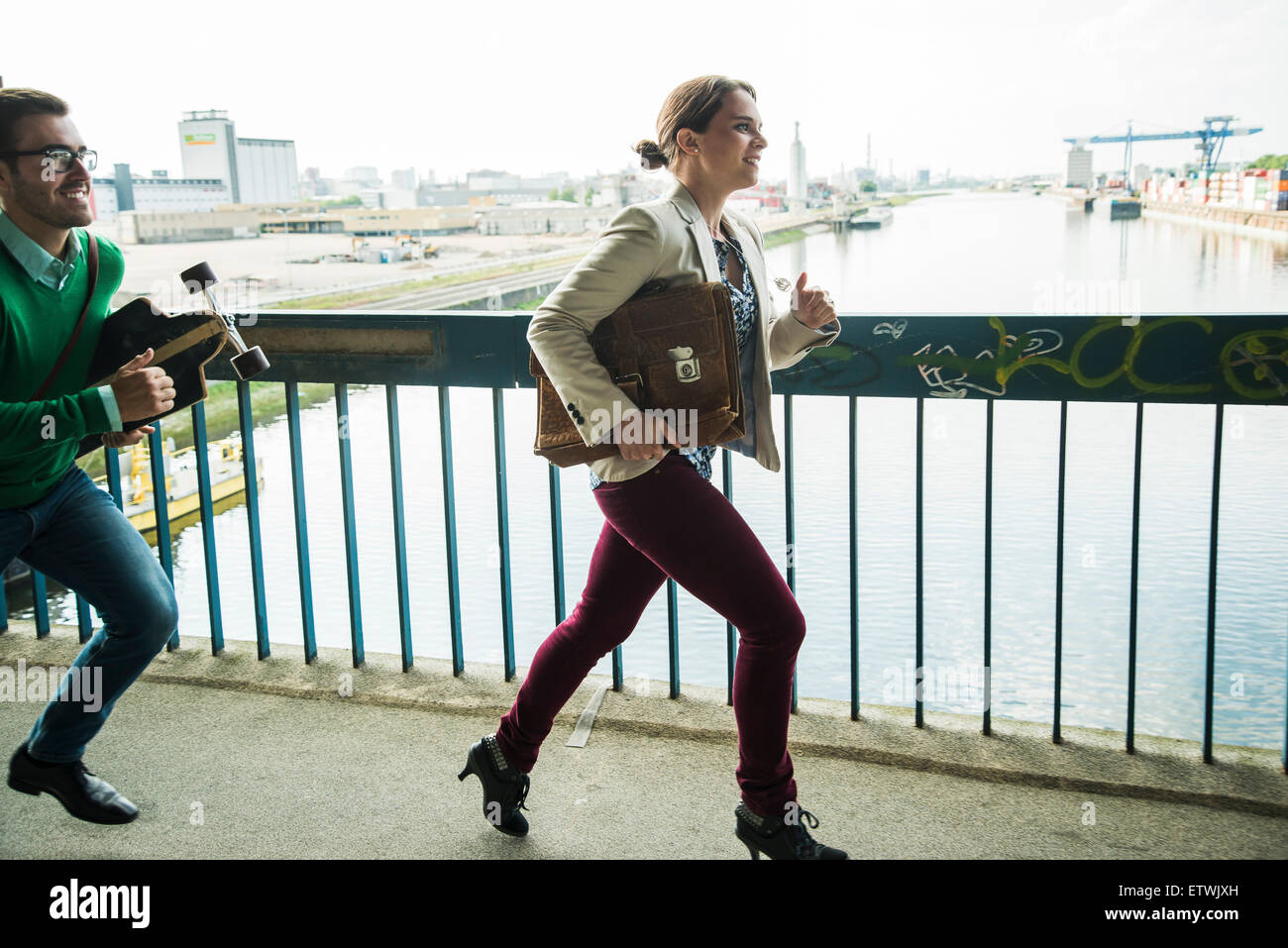 Young woman and man with skateboard running on bridge Stock Photo - Alamy