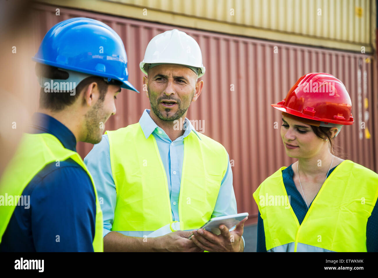 Woman and two men with safety helmets talking at container port Stock ...