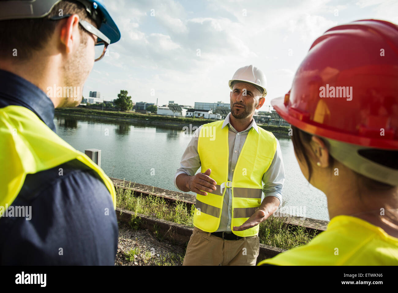 Woman and two men with safety helmets talking at riverside Stock Photo ...