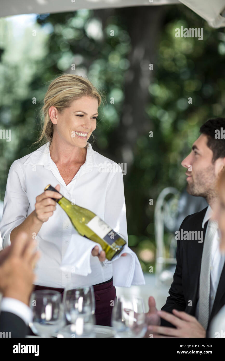 Waitress showing white wine to clients at table Stock Photo - Alamy