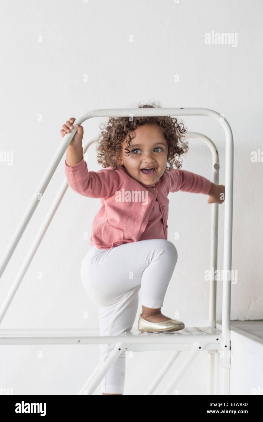 Little girl with curly hair climbing on ladder Stock Photo - Alamy