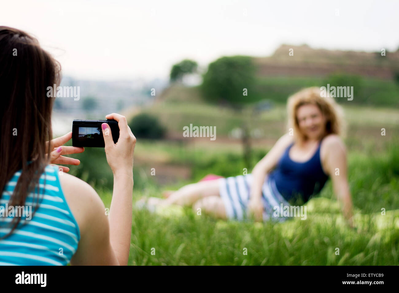 Girl photographing her girl friend, one is brunette and the other is ...