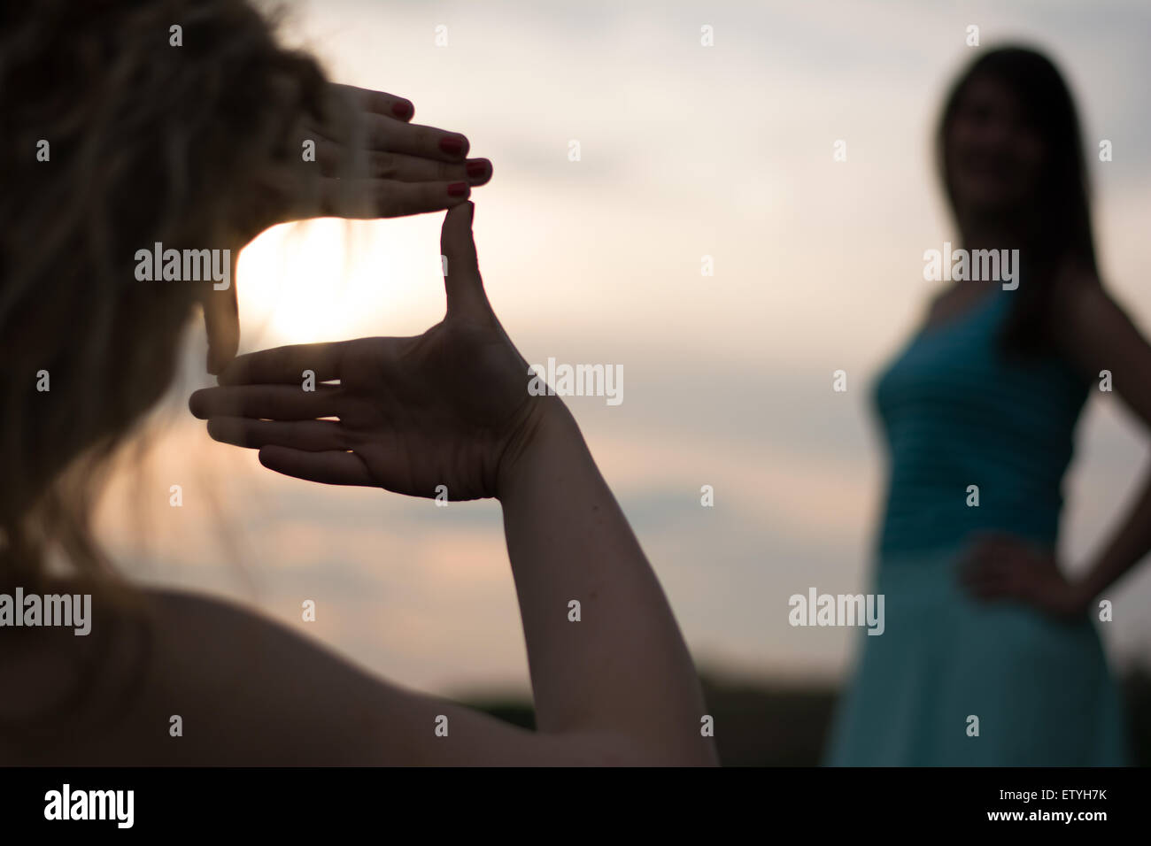Girl photographing her girl friend at sunset making camera out of hands ...