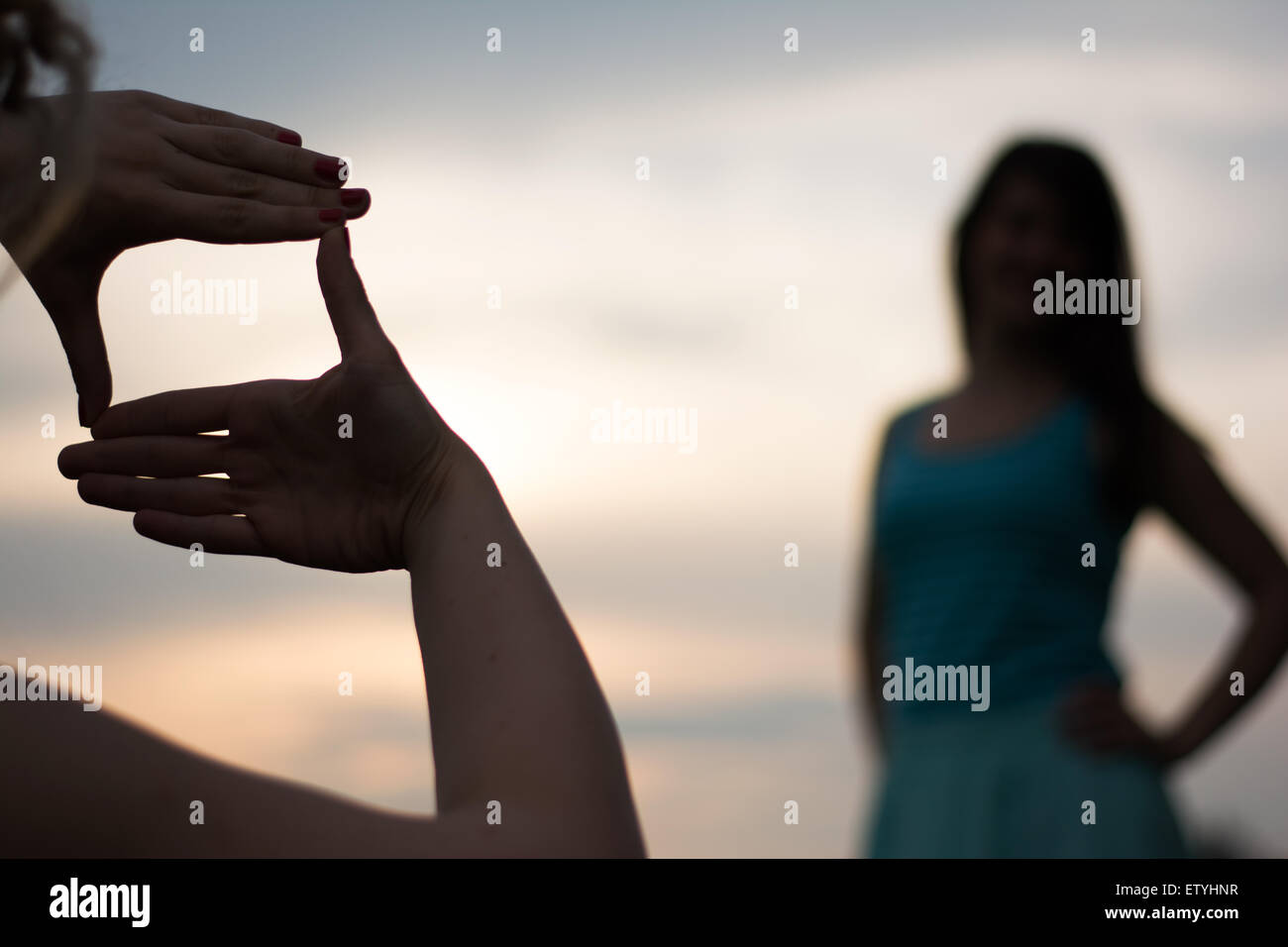 Girl photographing her girl friend at sunset making camera out of hands ...