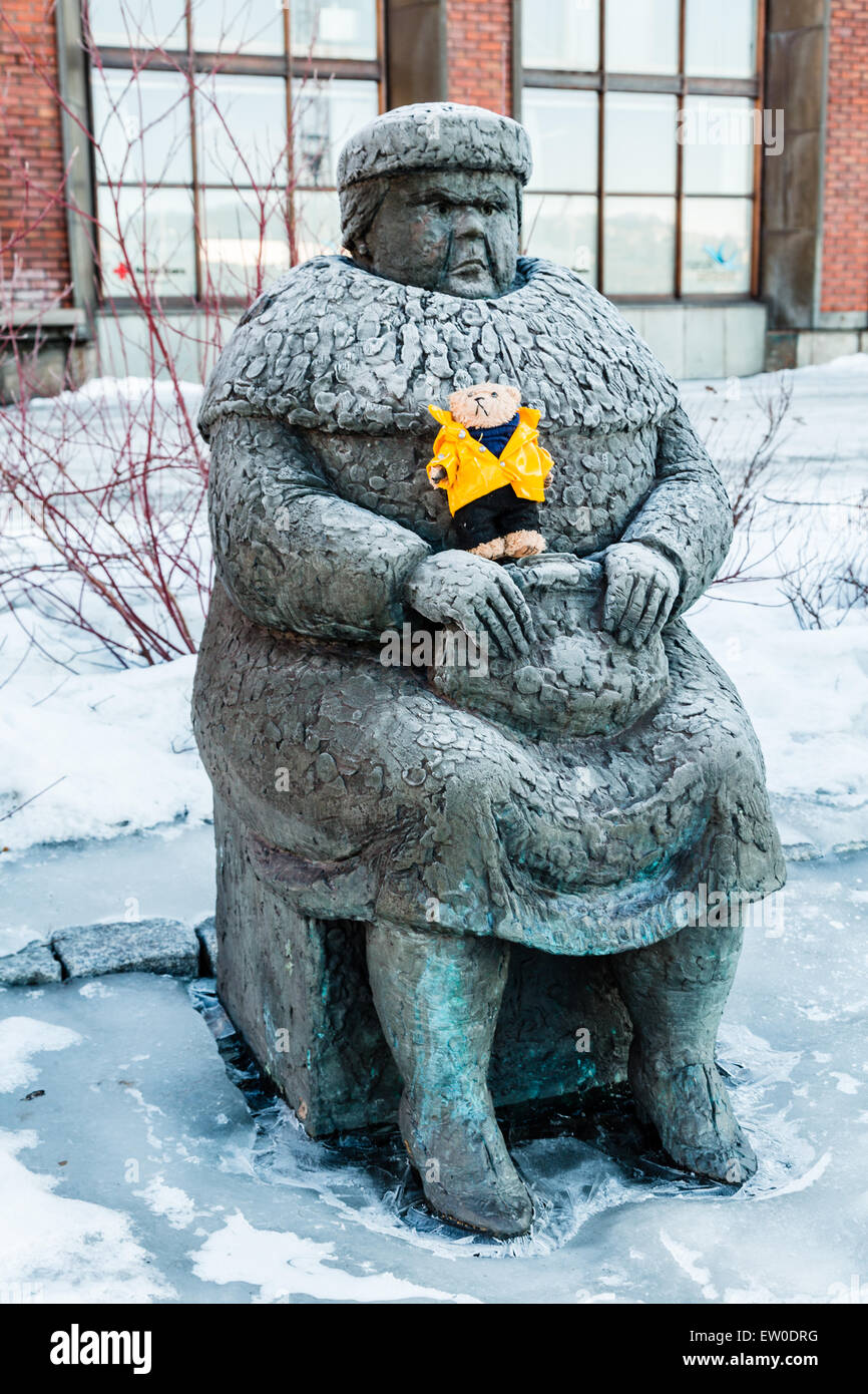 Beni, a teddy bear, standing on a statue of a grumpy looking woman in ...