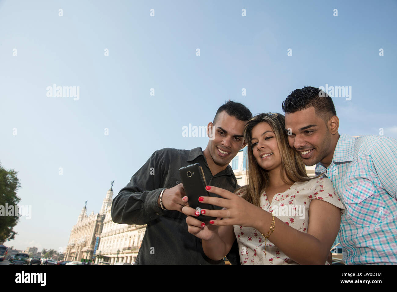 Three young Latin people using cell phone outdoors Stock Photo - Alamy