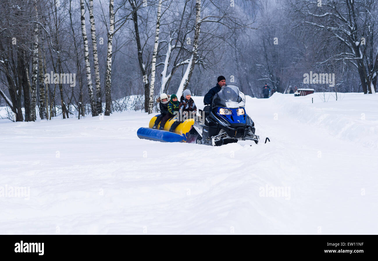 A snowmobile tows an inflatable sledge with three children on top in a ...