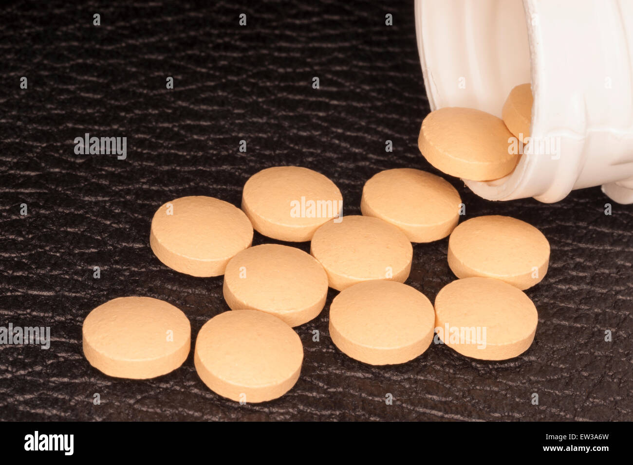 Tablet medications spilling from a white plastic bottle flowing onto ...