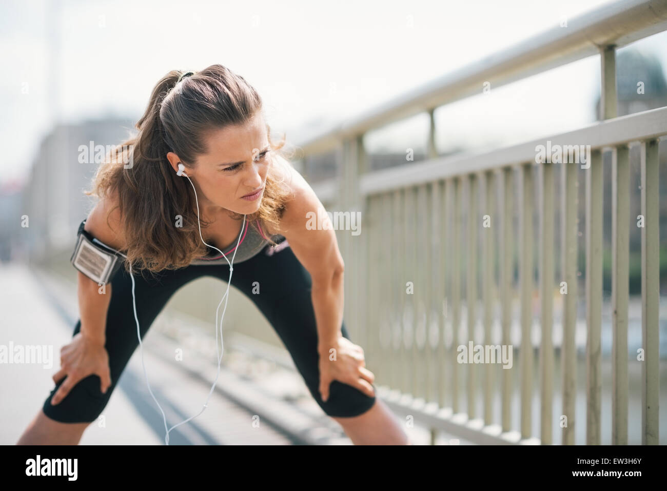 A woman jogger is taking a break, stretching her legs out by leaning ...