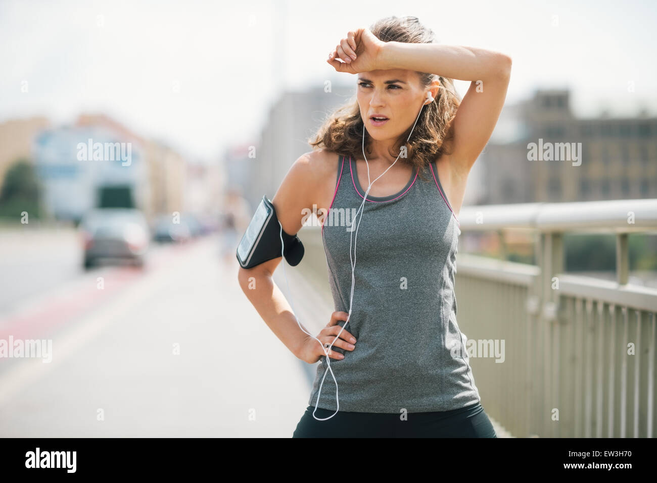A woman jogger is taking a break, wiping sweat from her forehead with ...