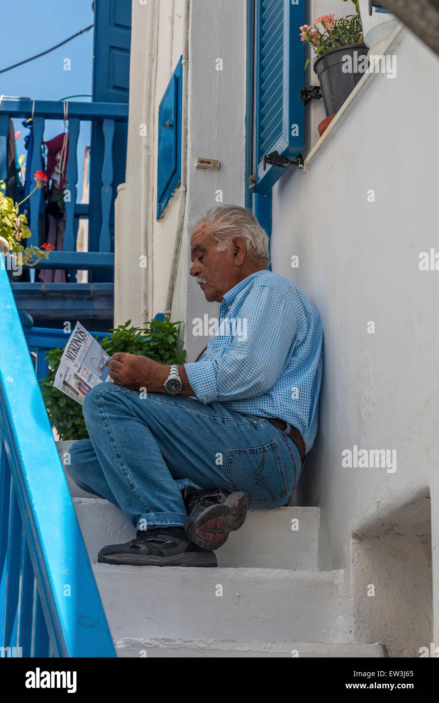 Greek man reading newspaper on the front steps of a traditional ...