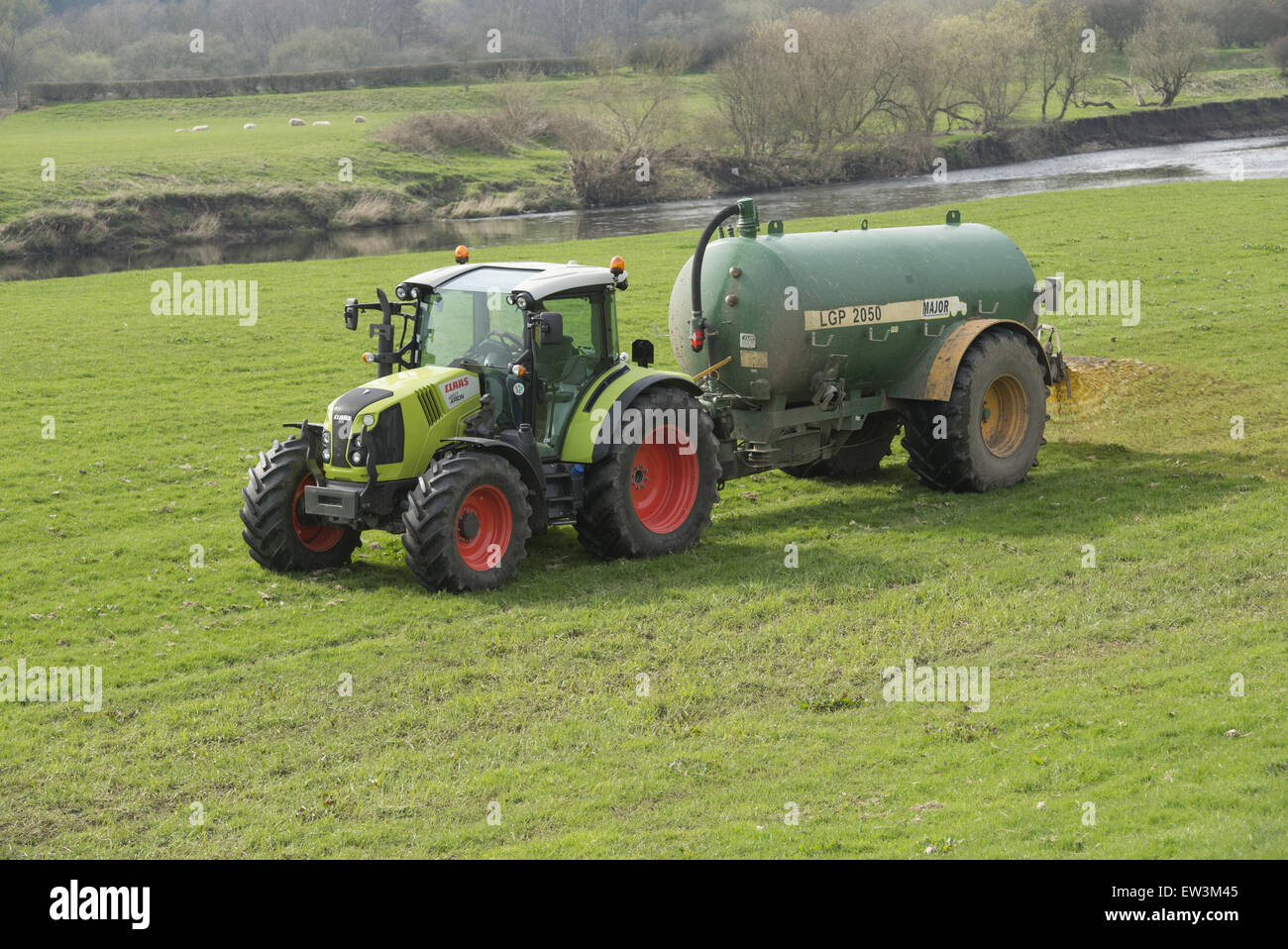 Claas tractor with slurry tanker, spreading slurry on grassland near ...