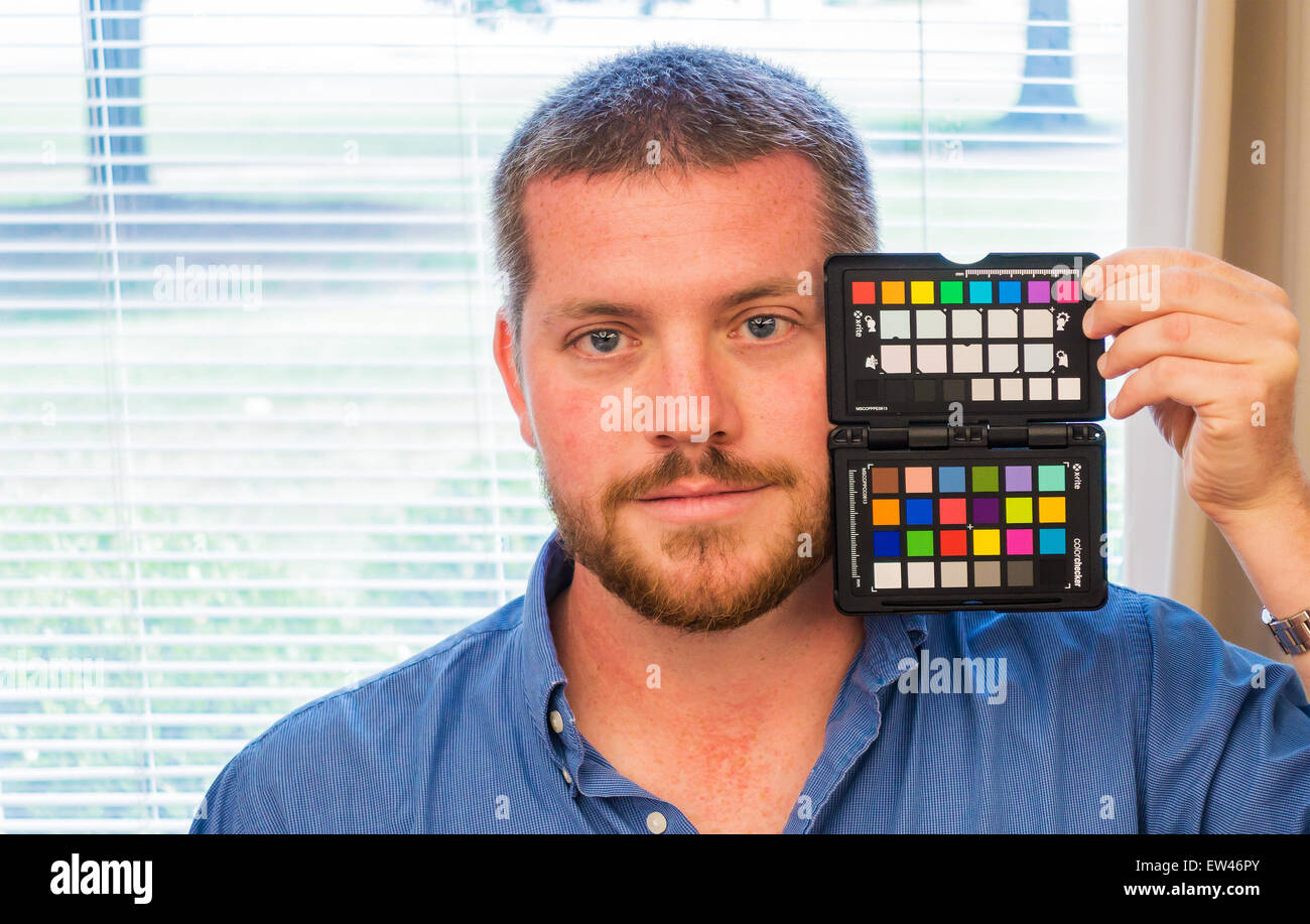 A 28 year old Caucasian man holds an xrite color checker near his face ...