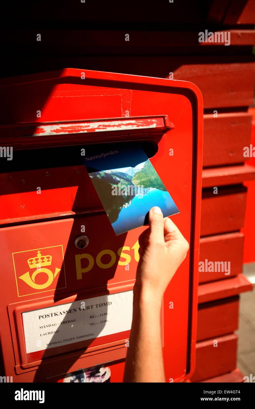 A woman puts a postcard into a red mail box in the Fyords in Norway ...