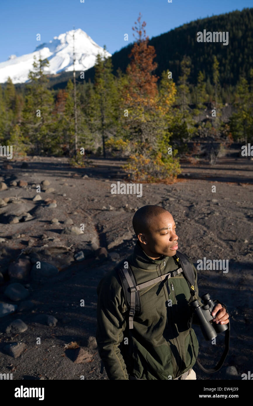 African American man Cupid Alexander stands with binoculars in forest ...