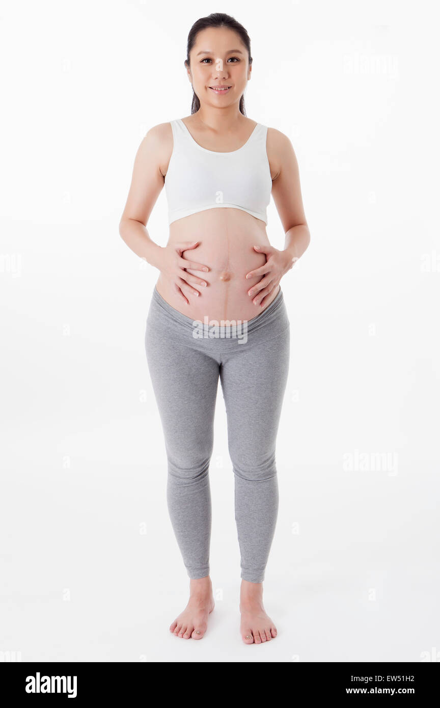 Pregnant woman standing and smiling at the camera with hands on abdomen ...