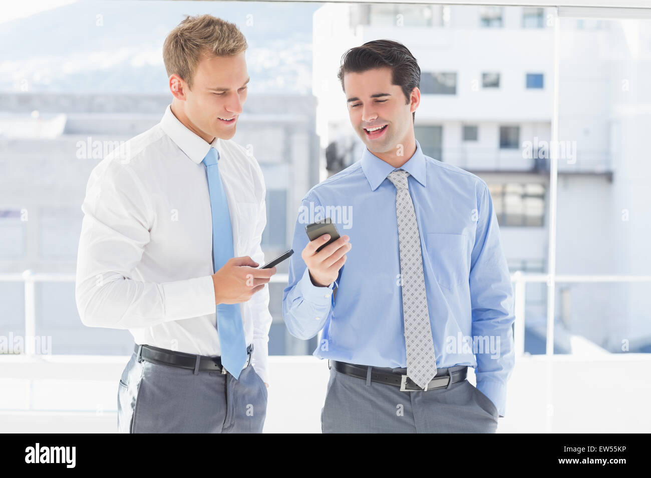 Two businessmen talking to each other and texting Stock Photo - Alamy