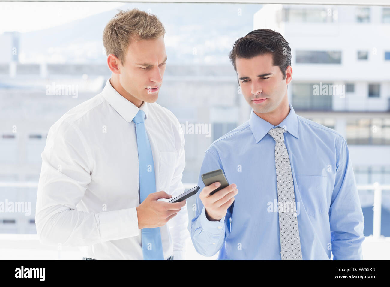 Two businessmen talking to each other and texting Stock Photo - Alamy