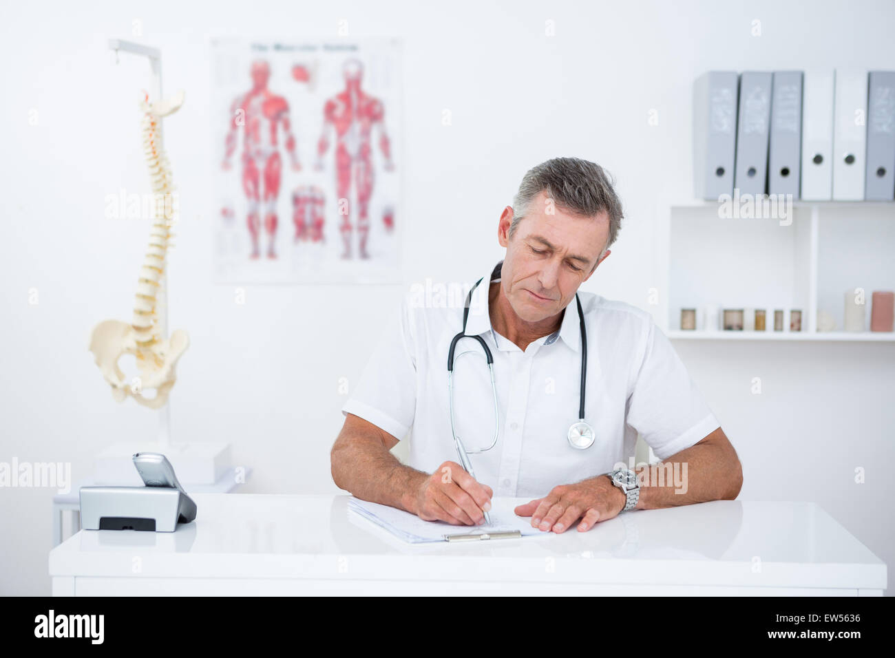 Doctor writing on clipboard at his desk Stock Photo - Alamy
