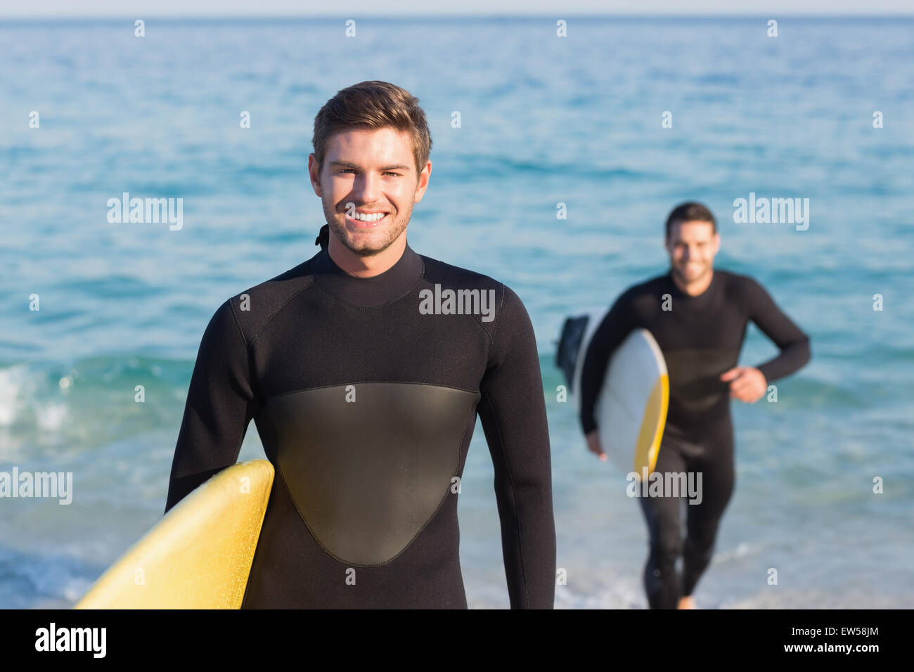Two men in wetsuits with a surfboard on a sunny day Stock Photo - Alamy