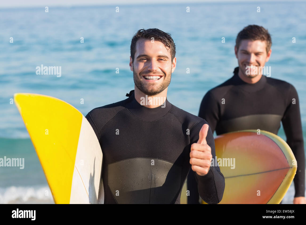 Two men in wetsuits with a surfboard on a sunny day Stock Photo - Alamy