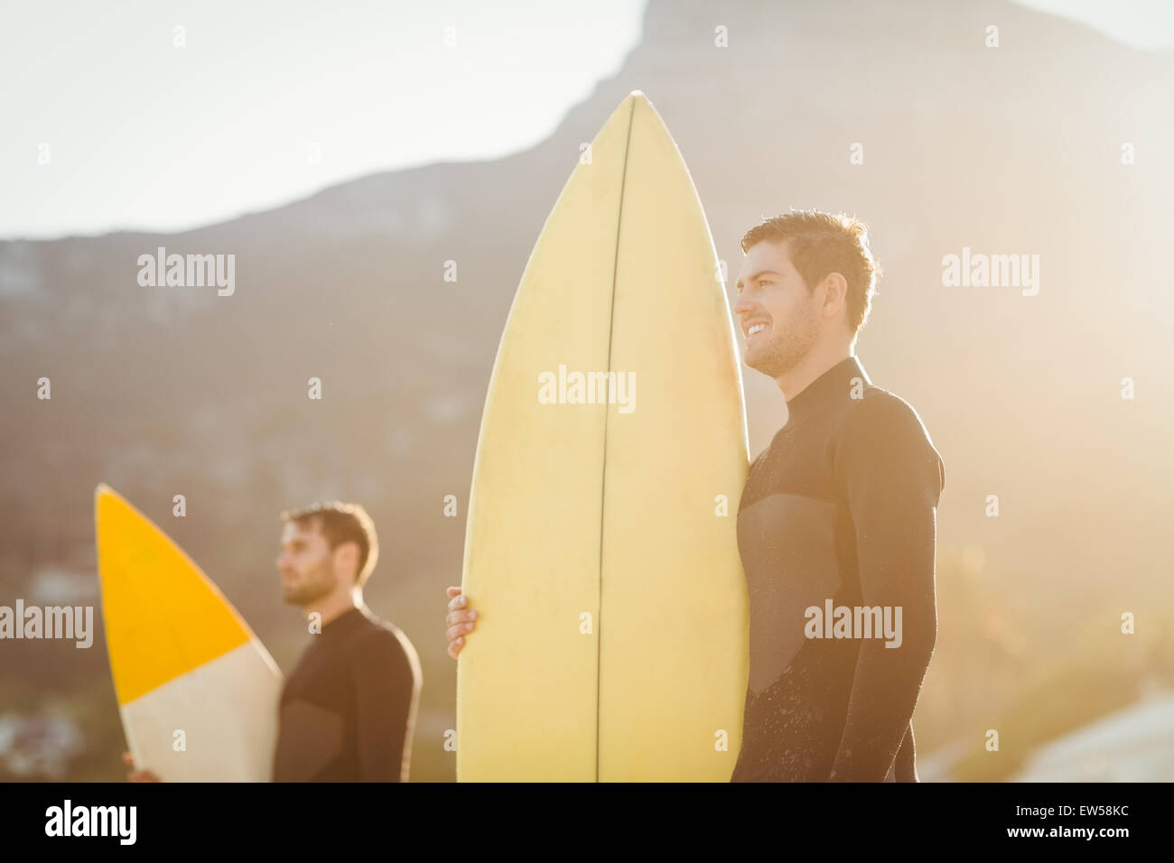 Two men in wetsuits with a surfboard on a sunny day Stock Photo - Alamy