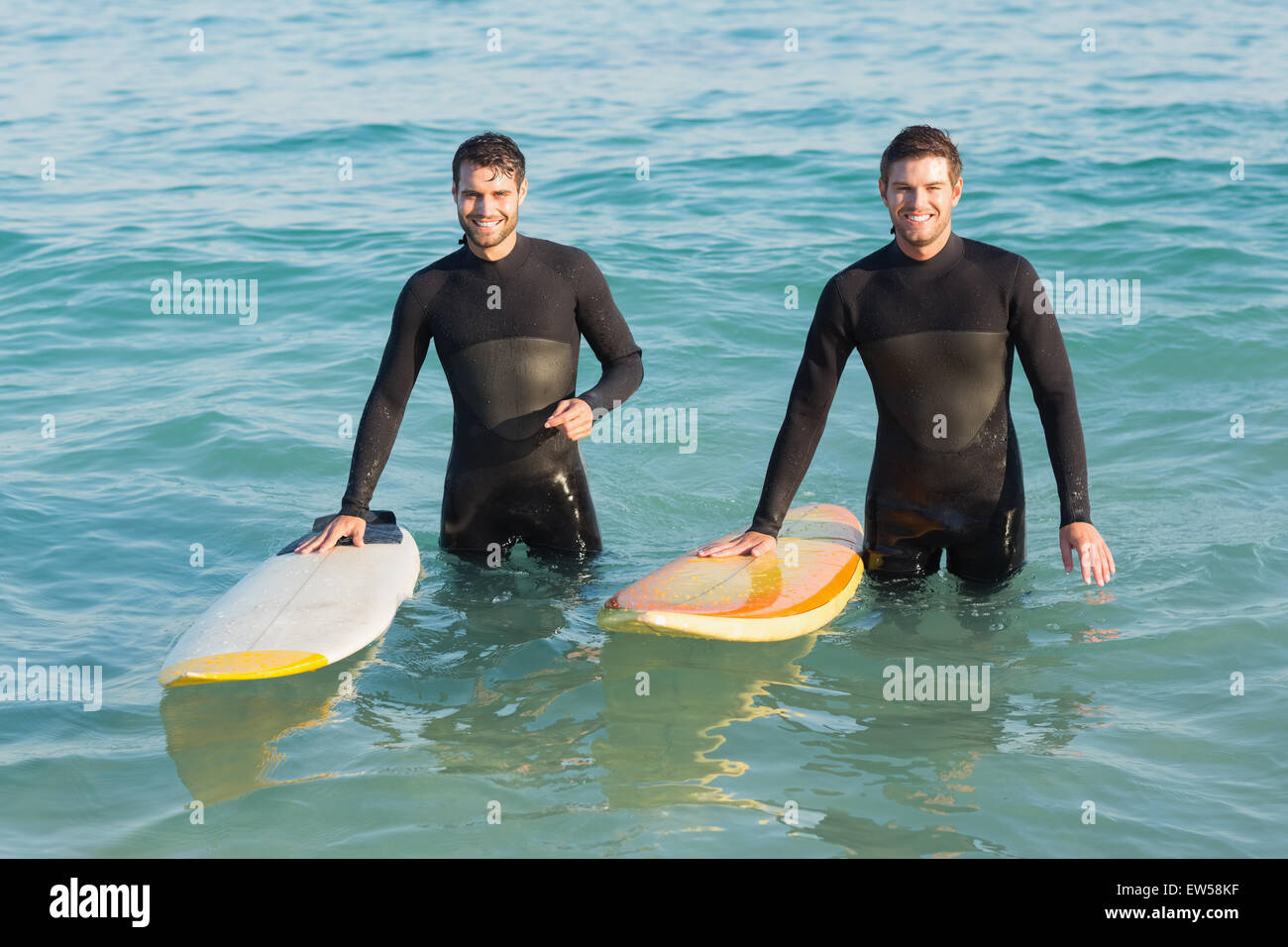 Two men in wetsuits with a surfboard on a sunny day Stock Photo - Alamy