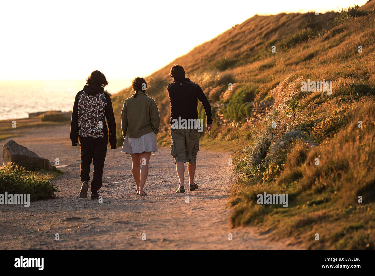 Three people walking into the evening light on the coastal path around ...