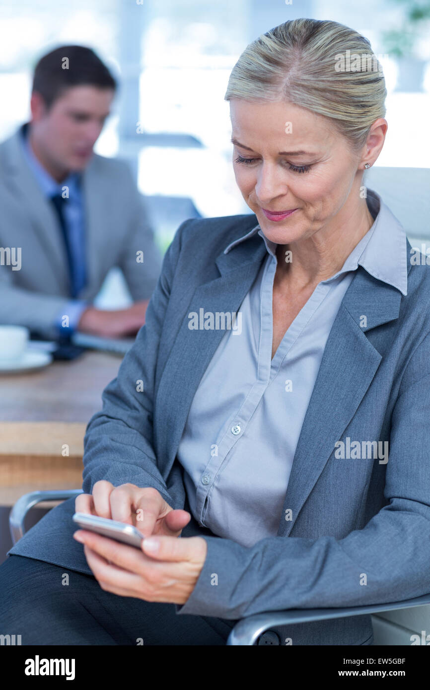 Businesswoman texting on her mobile phone with colleague in background ...