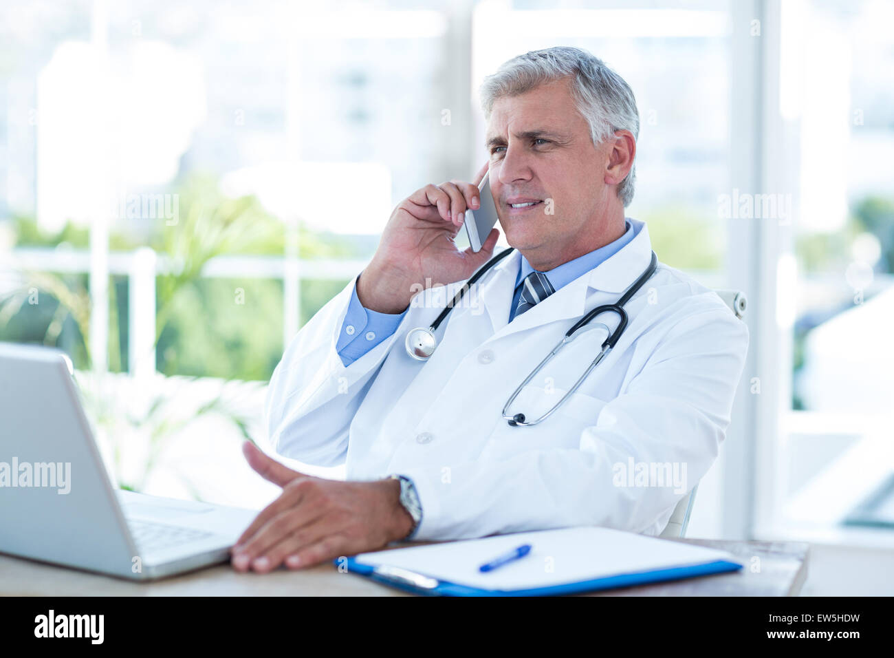 Smiling doctor having phone call at his desk Stock Photo - Alamy