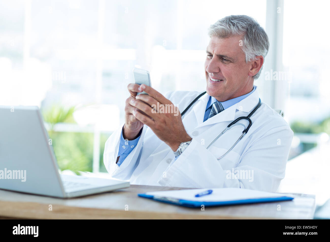 Smiling doctor sitting at his desk and texting Stock Photo - Alamy