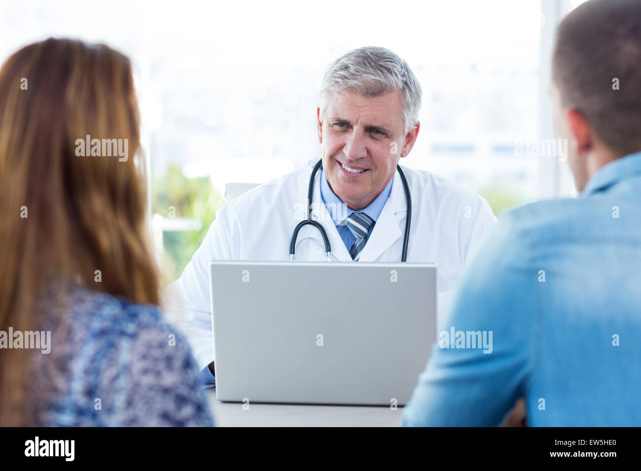 Smiling doctor talking to happy couple Stock Photo - Alamy
