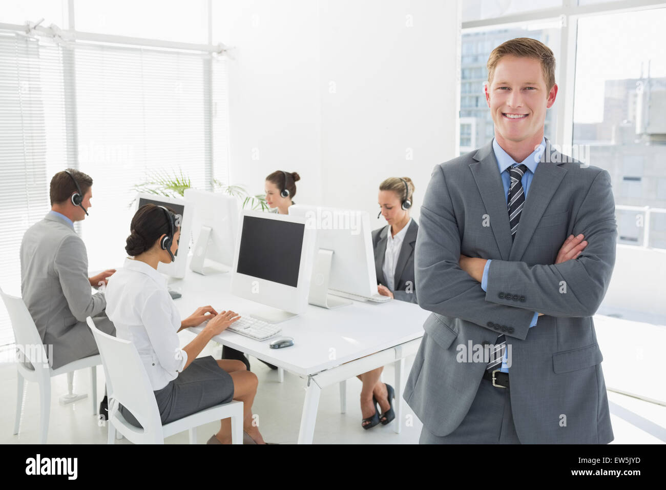 Smiling manager standing arms crossed with staff behind Stock Photo - Alamy