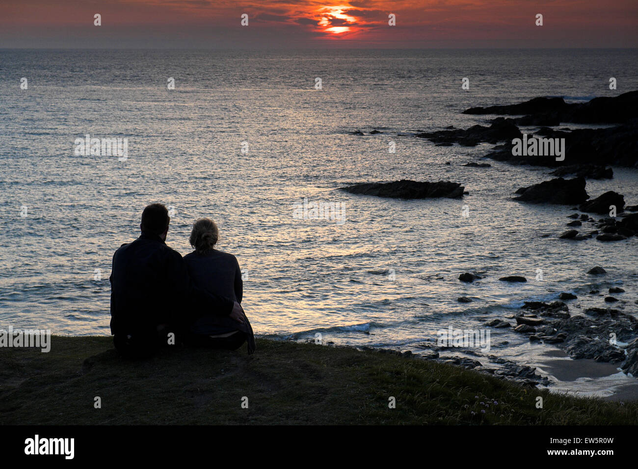 A couple gazing at the sunset on the rugged coast of Newquay in ...