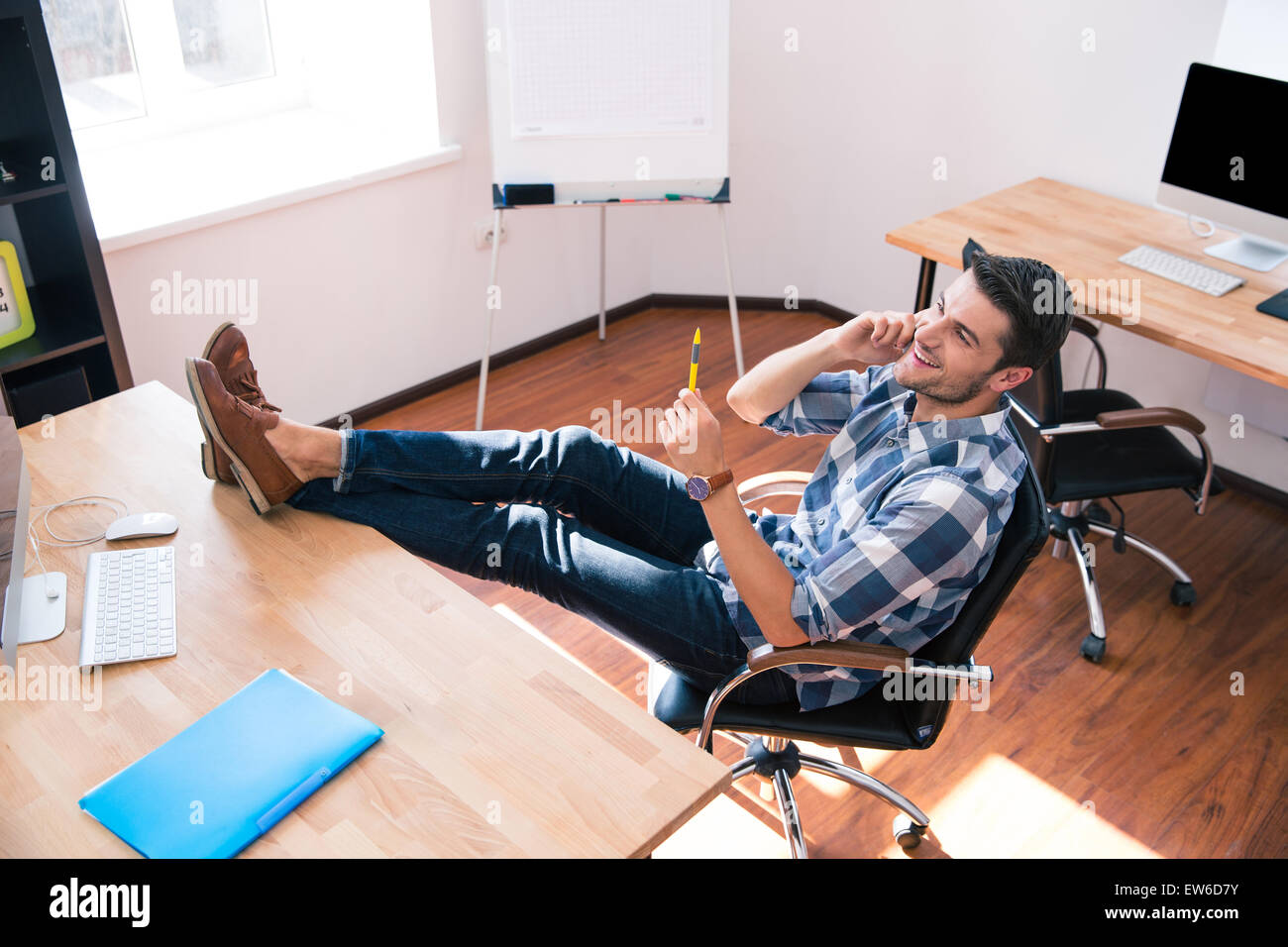 Happy businessman sitting on the office chair and talking on the phone ...