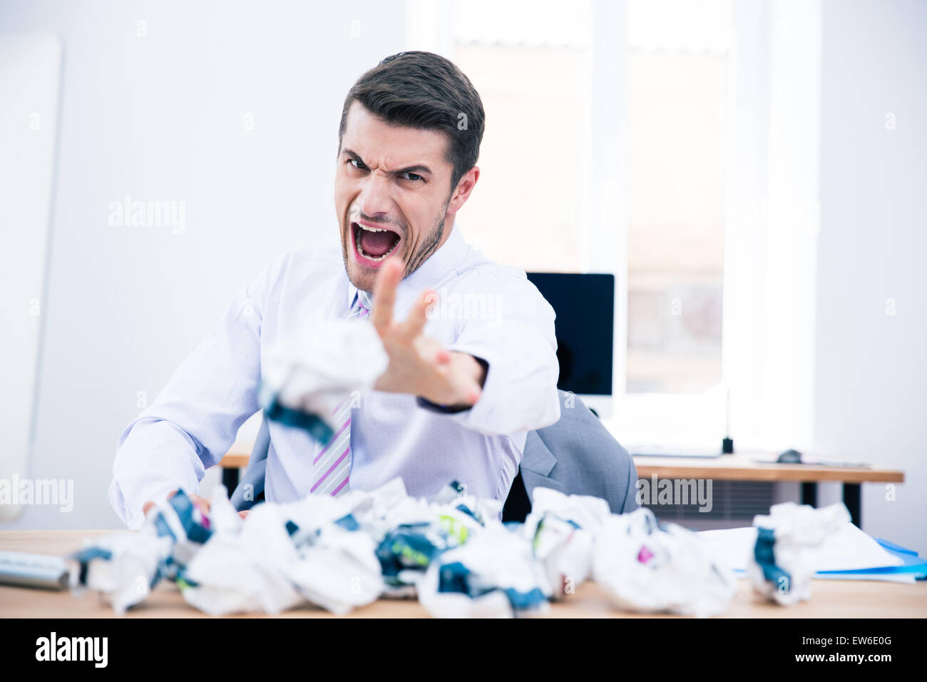 Angry businessman sitting at the table and throwing crumpled paper on ...